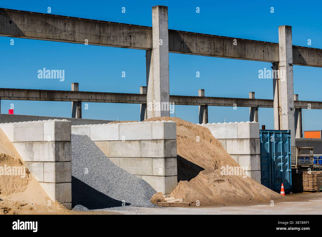 Large piles of sand and gravel are stored against concrete structures ...
