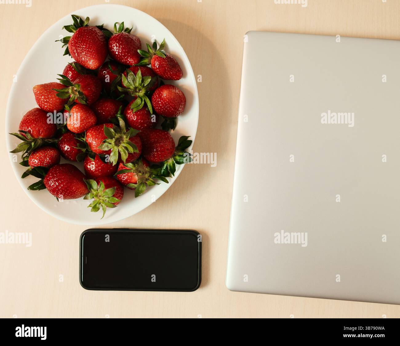 A white bowl of glossy red strawberries sits beside a sleek smartphone ...