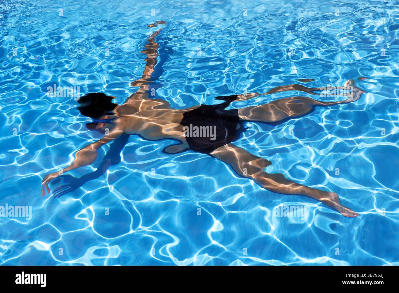 Man swimming underwater with light ripples reflecting in blue water of ...