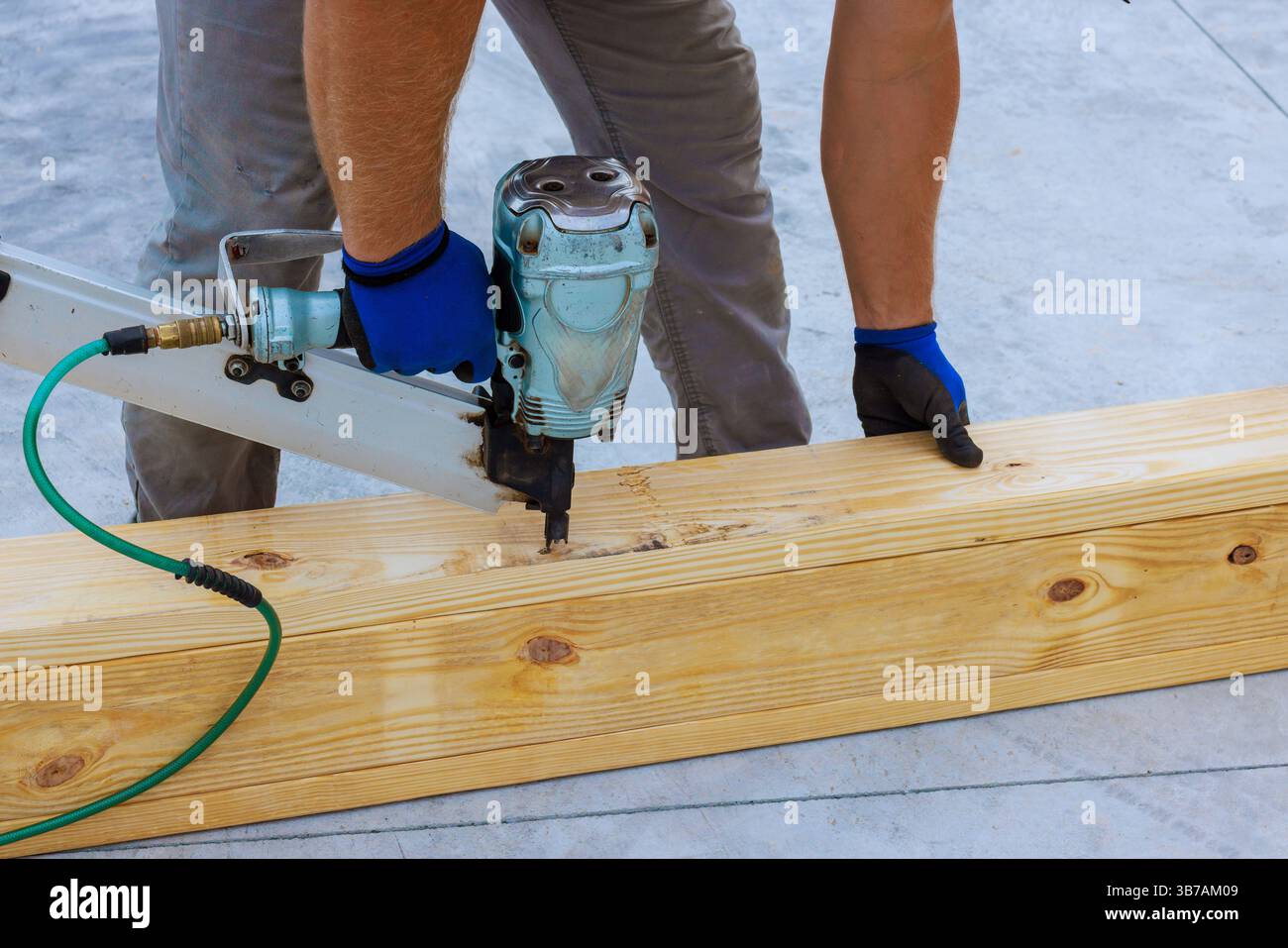 Worker drives nails into wooden beam using air nail gun on construction ...