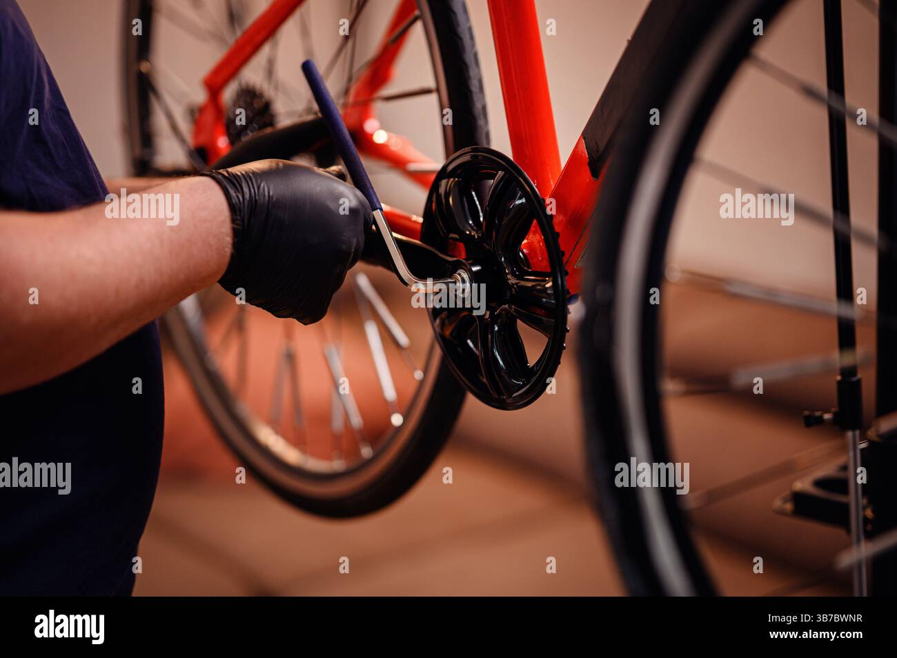 Gloved hands use a tool to attach a crank arm to a red bikes bottom ...