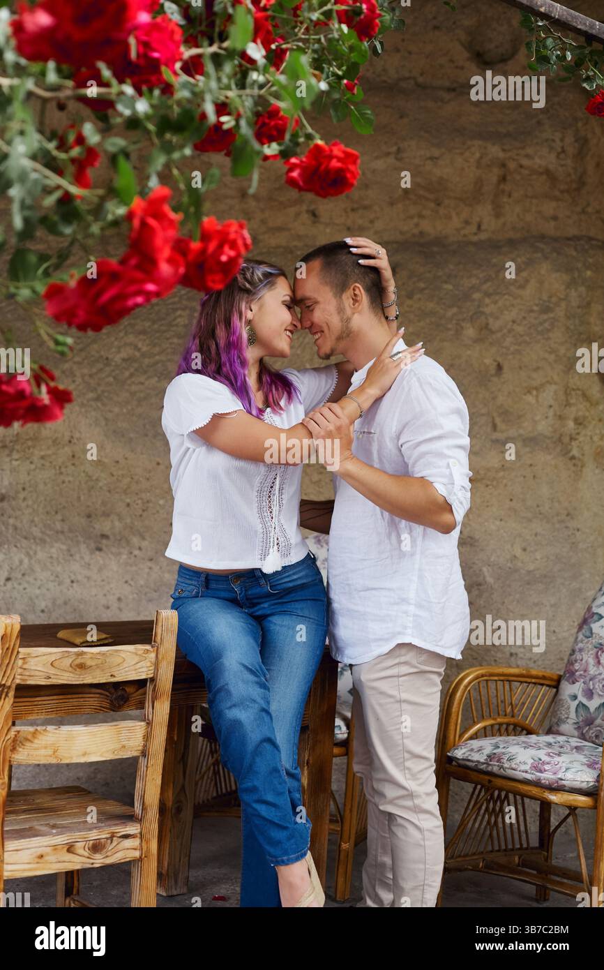 young couple shares a tender moment while standing beneath vibrant rose ...