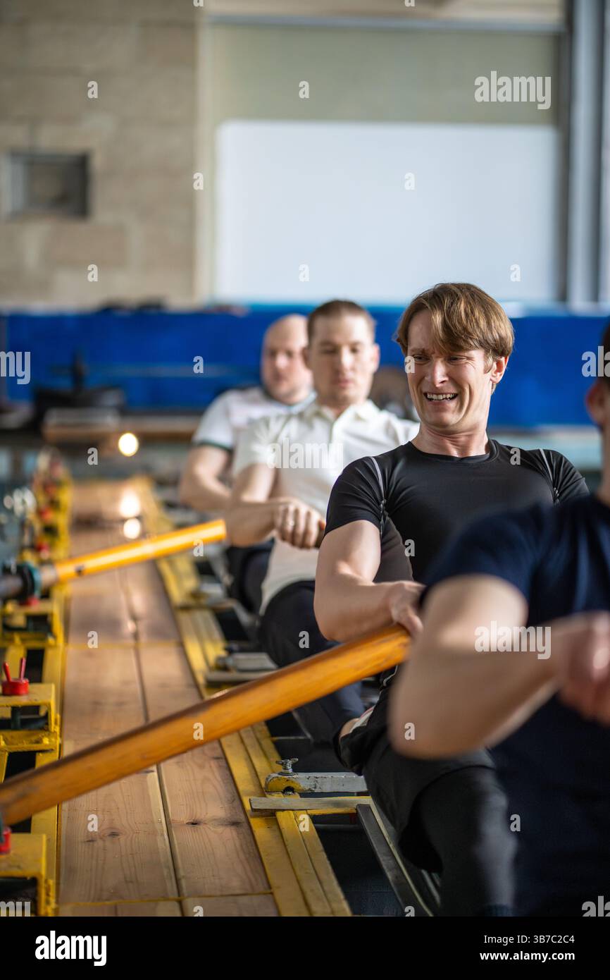 Struggling grimacing sportsmen exert on rowing simulator, paddling ...