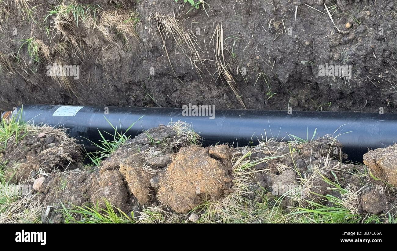 Black pipe installation in suburban trench with exposed soil and grass ...