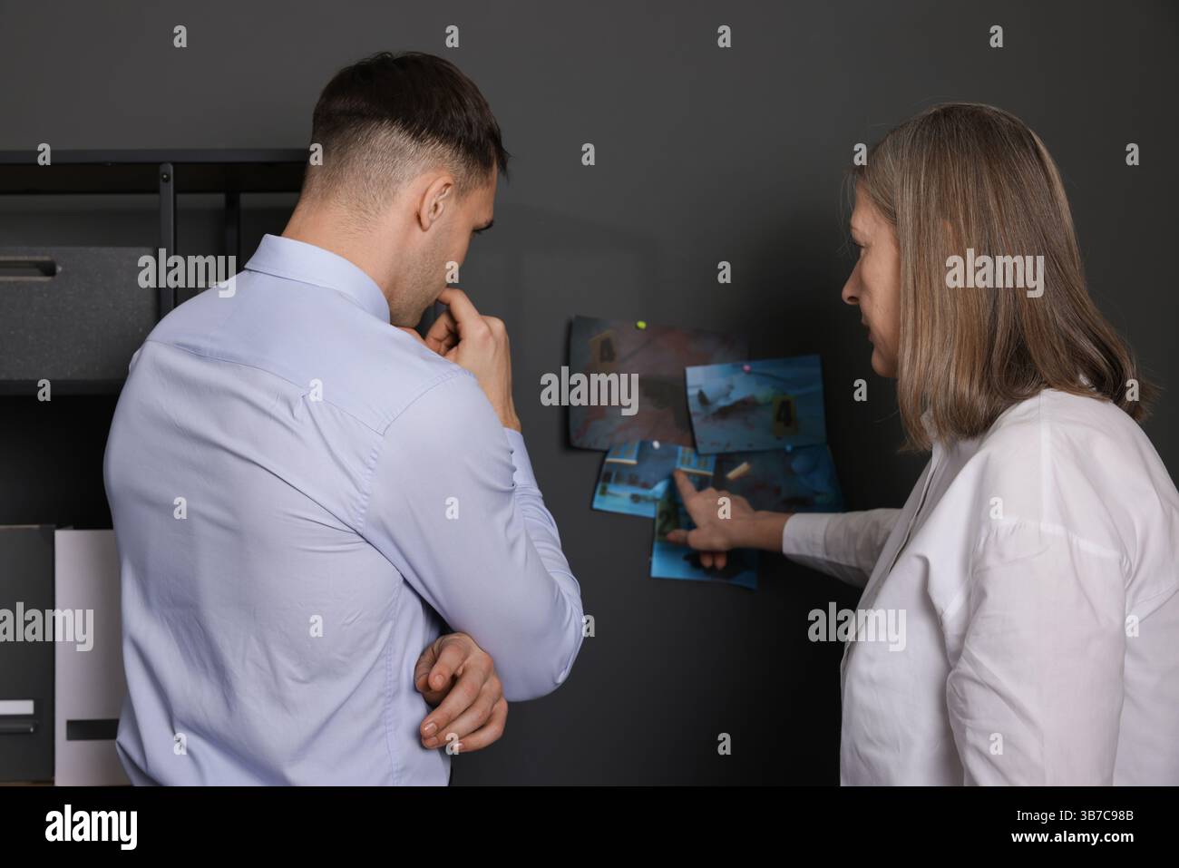 Forensic experts working with crime scene photos in office, back view ...