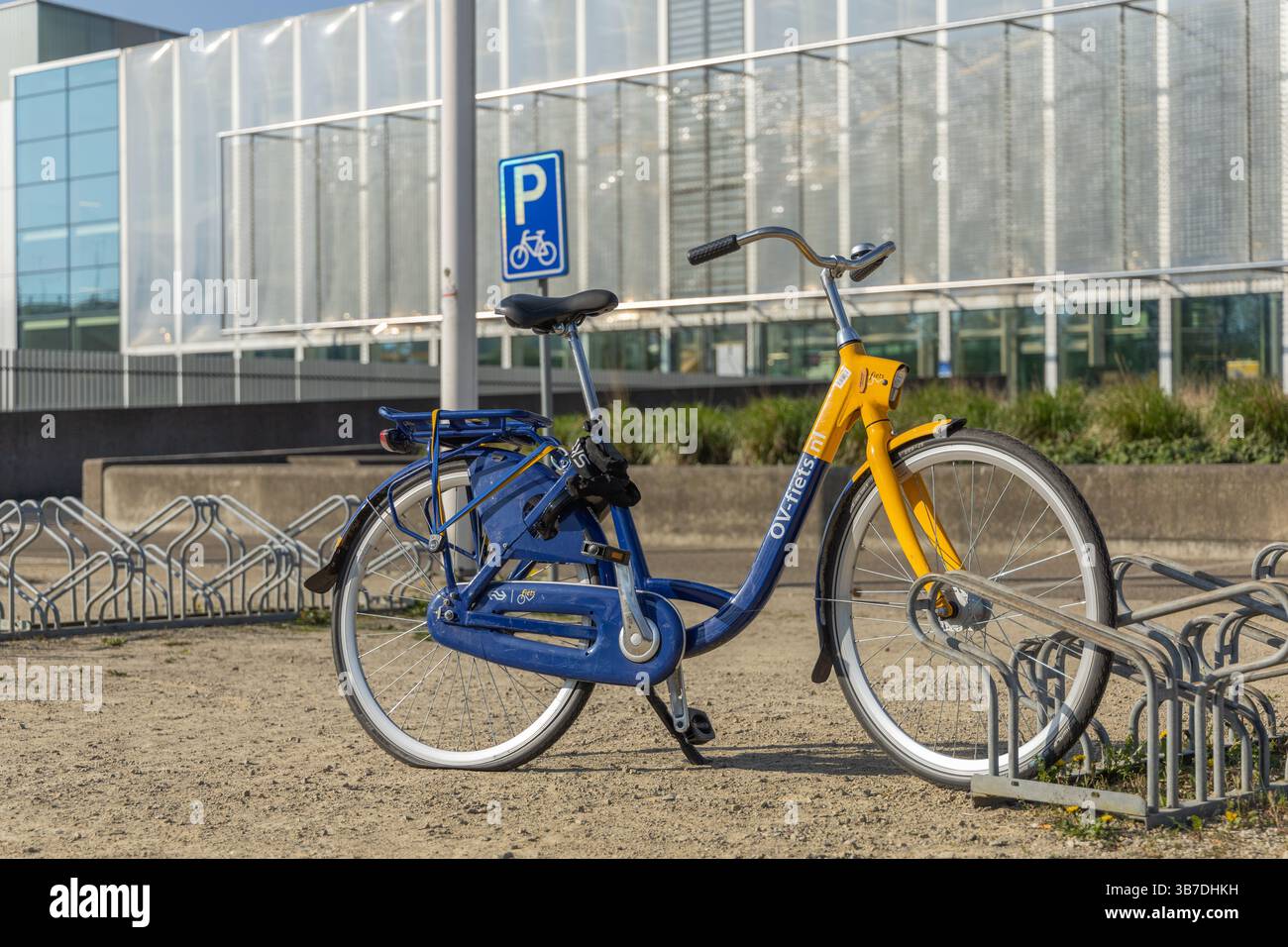 A blue and yellow OV-fiets rental bicycle is parked in a metal rack on ...