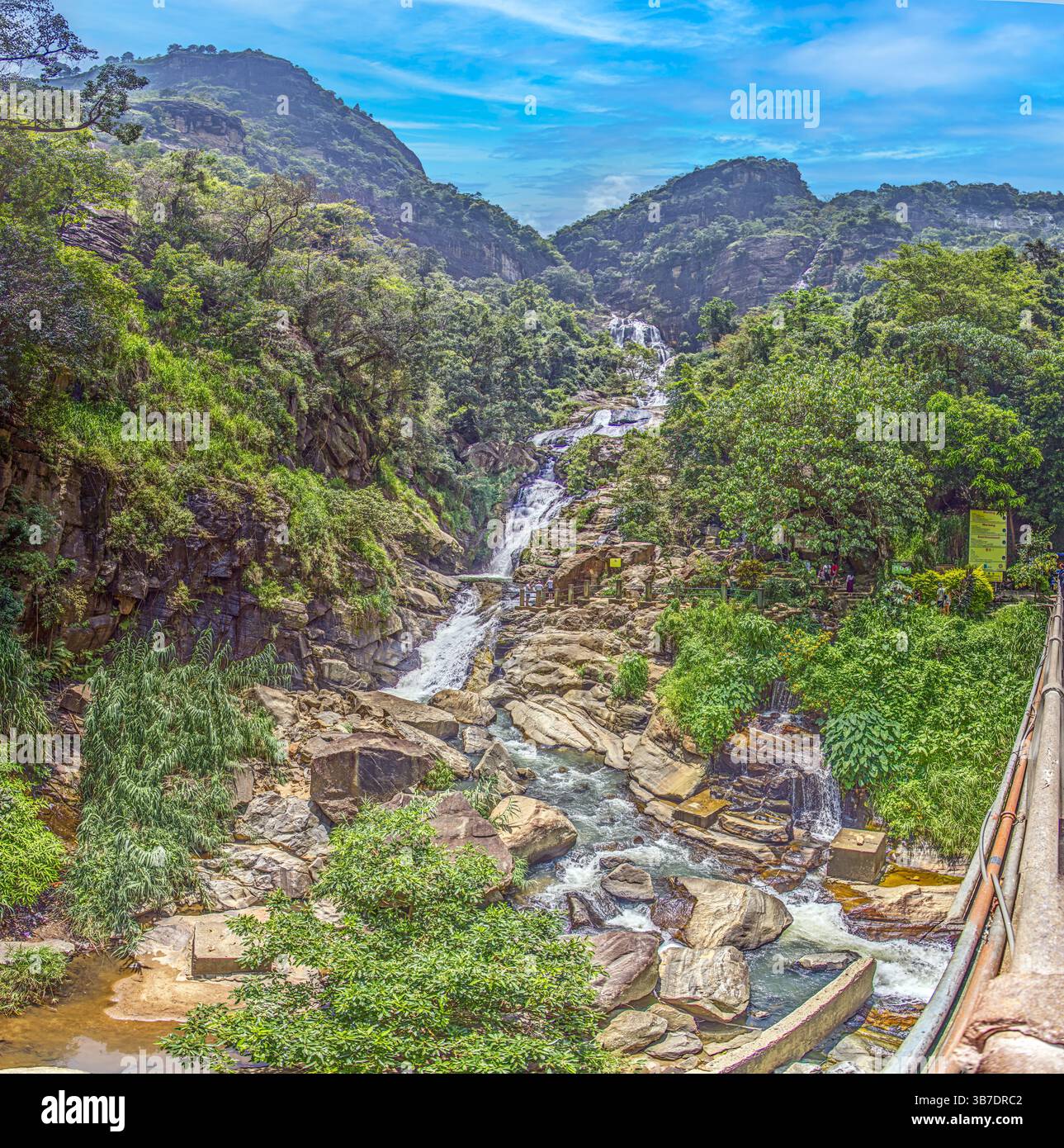 The tall Diyaluma waterfall cascades down a steep rocky slope in lush ...