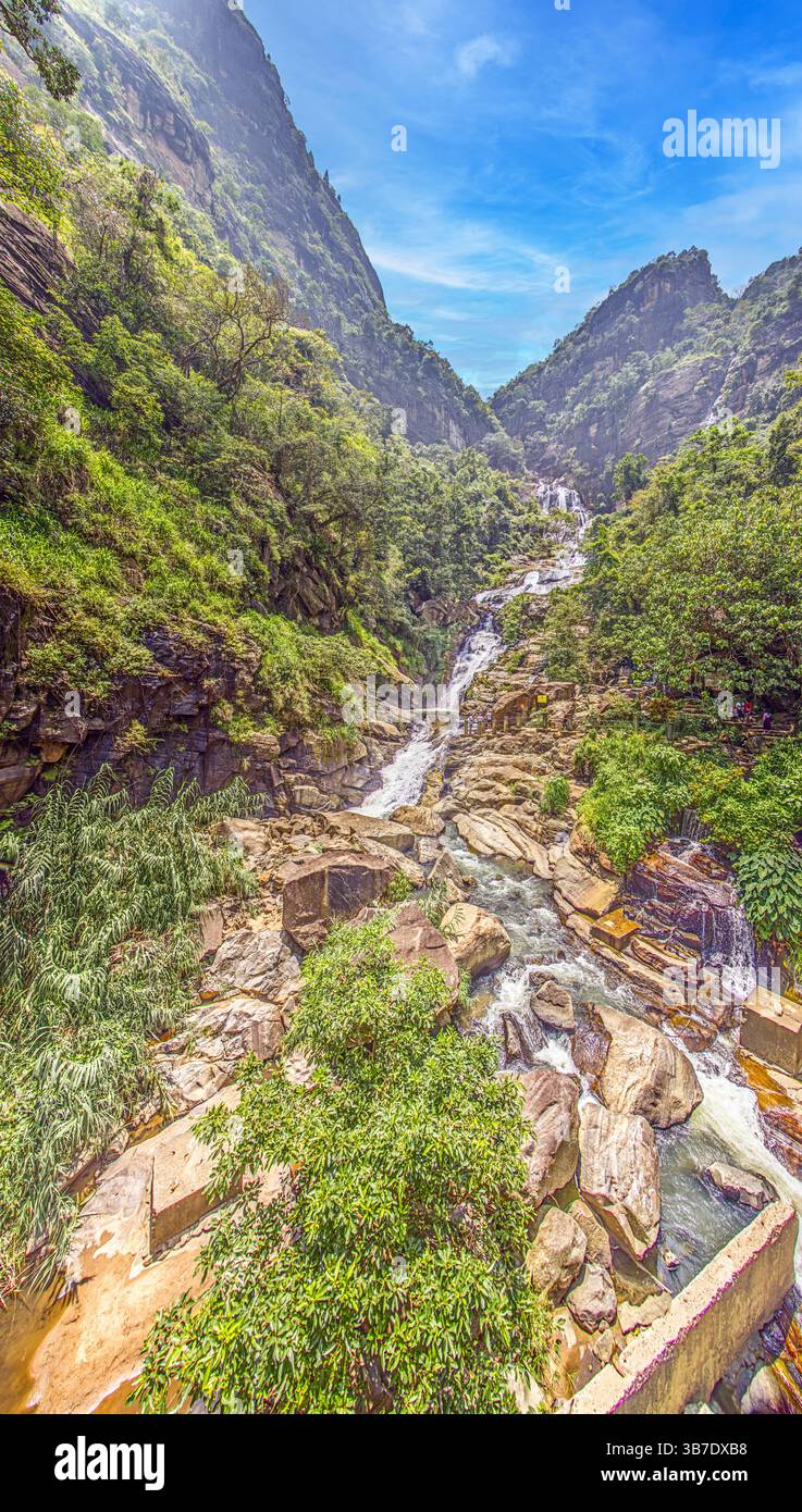 The tall Diyaluma waterfall cascades down a steep rocky slope in lush ...
