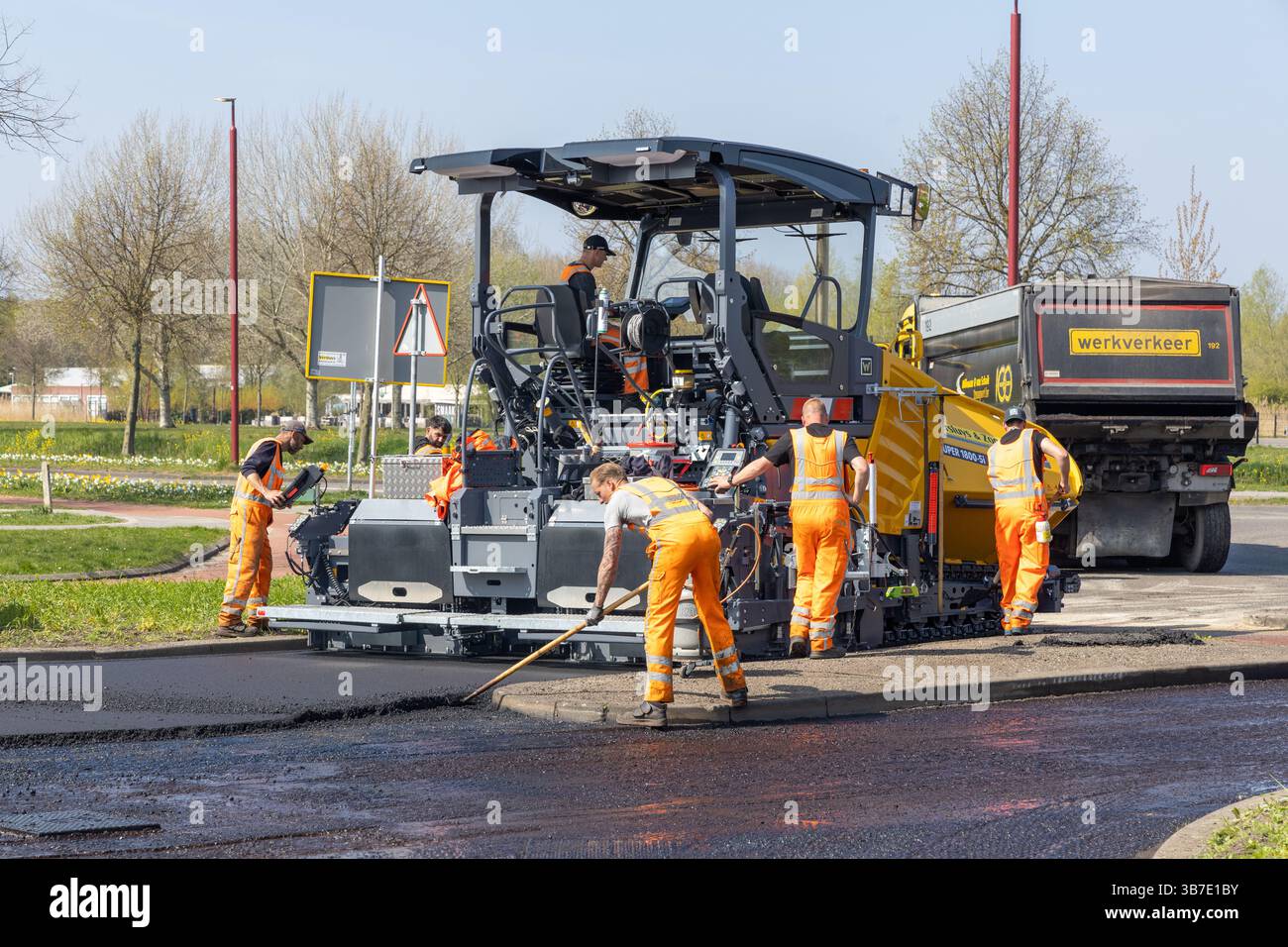 Road construction workers operate heavy machinery to lay fresh asphalt ...