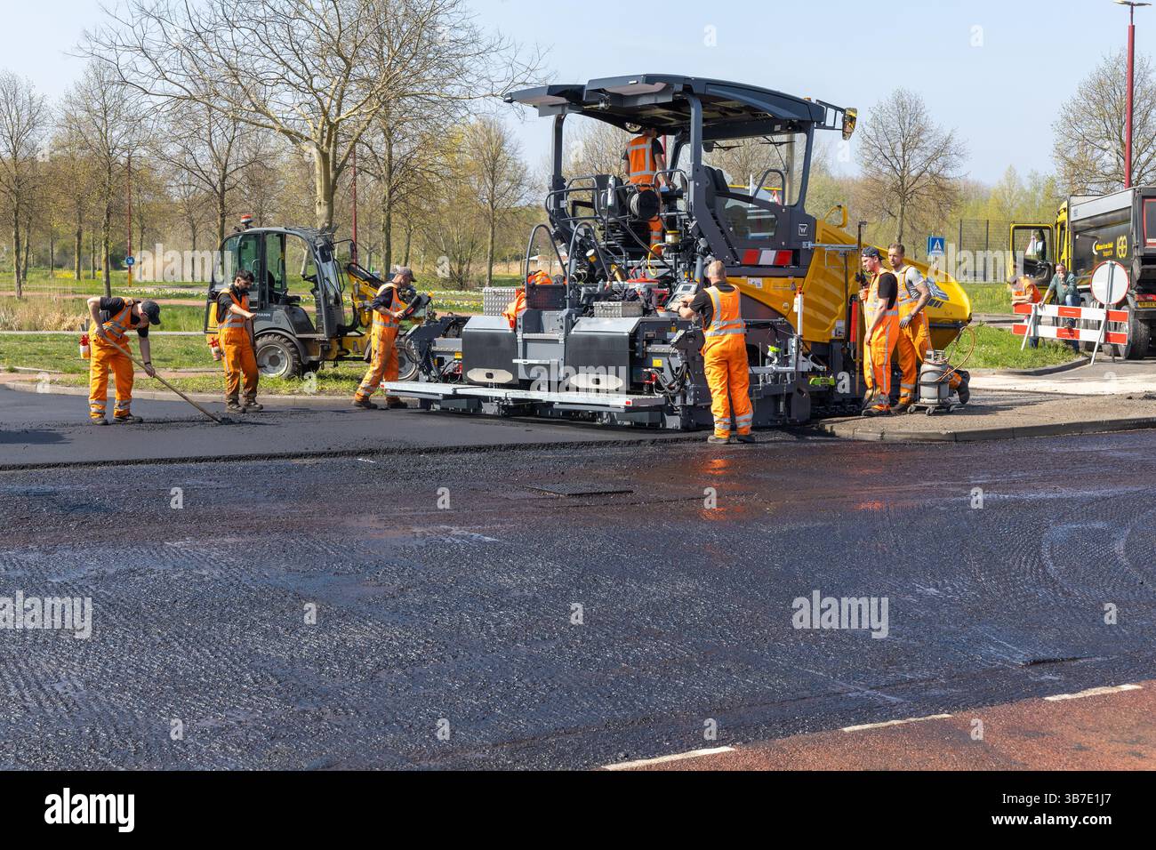 Road construction crew and machinery, including a paver, work on laying ...