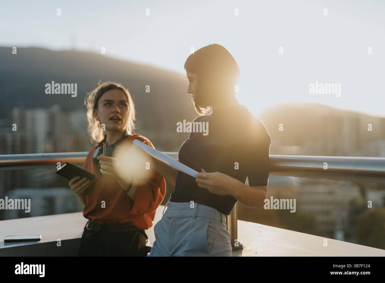Two diverse colleagues engage in a brainstorming session at sunset ...
