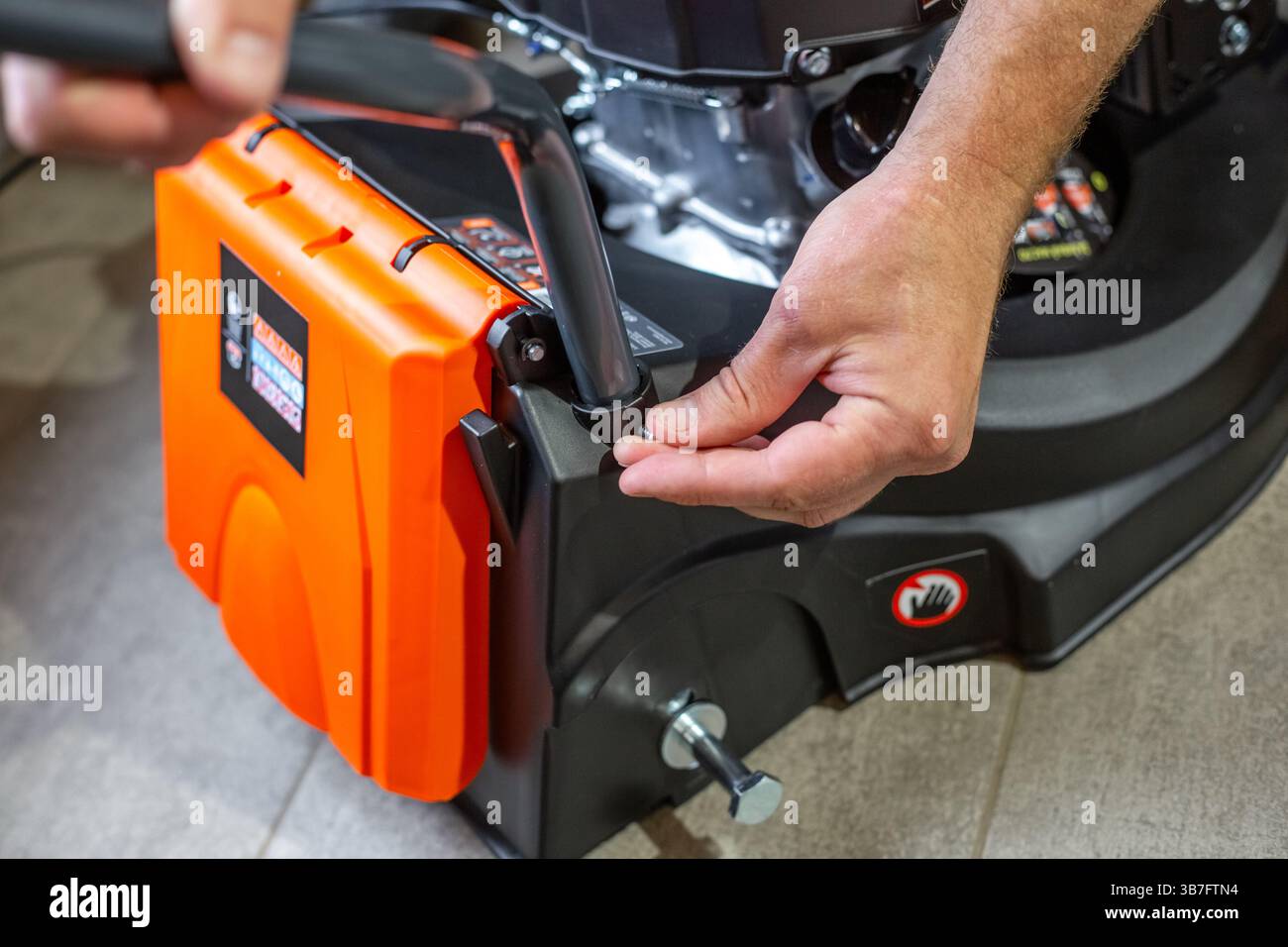Assembling a petrol lawn mower. A man secures the drive control handle ...