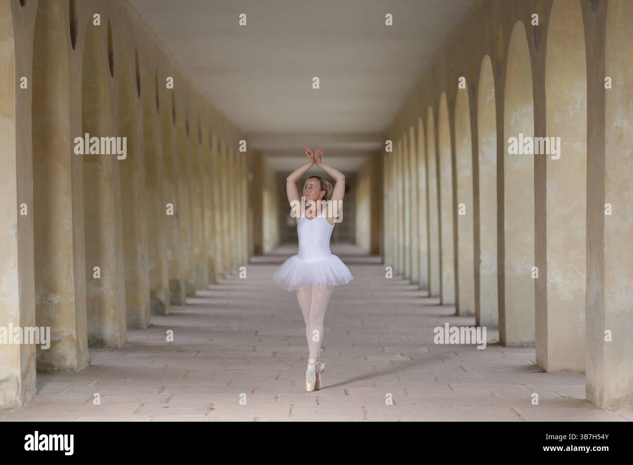Ballerina dances in perfect symmetry in a light-flooded corridor with ...