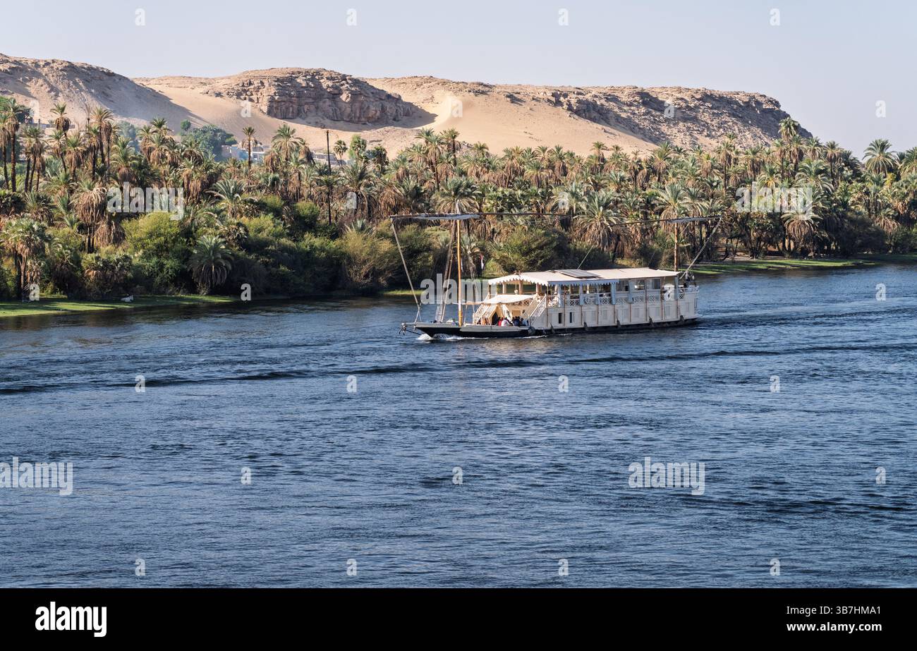Dahabiya Nile cruise ship sailing alongside a sandy desert with palm ...