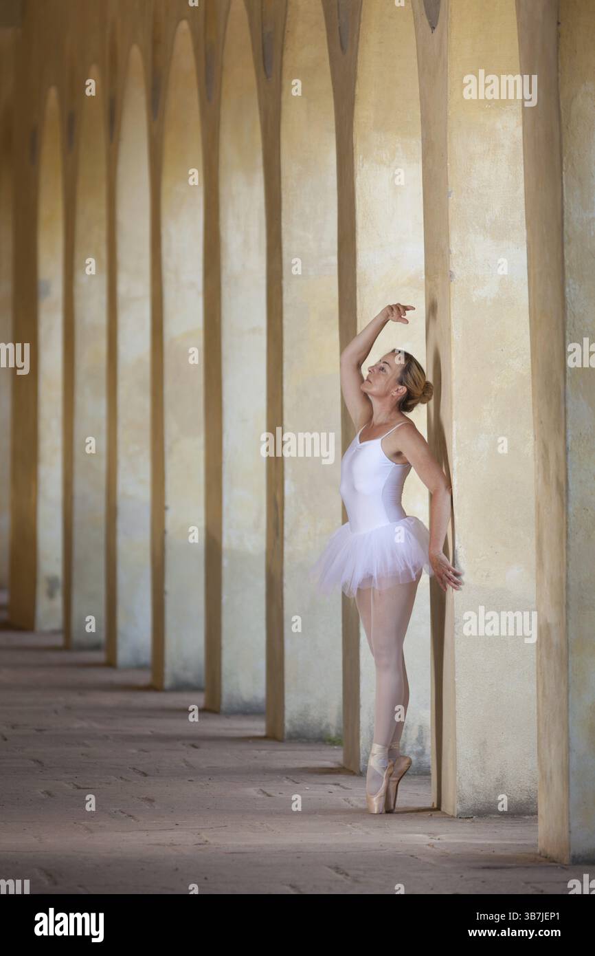 Ballerina in a white tutu poses elegantly against yellowish arcade ...
