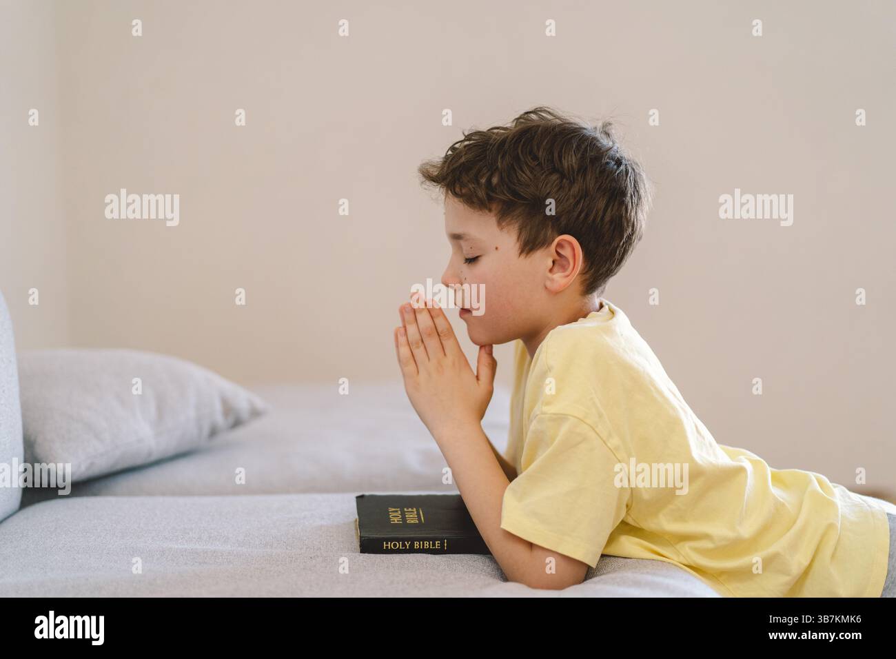 A boy with folded hands in front of him, he prays in his room Stock ...