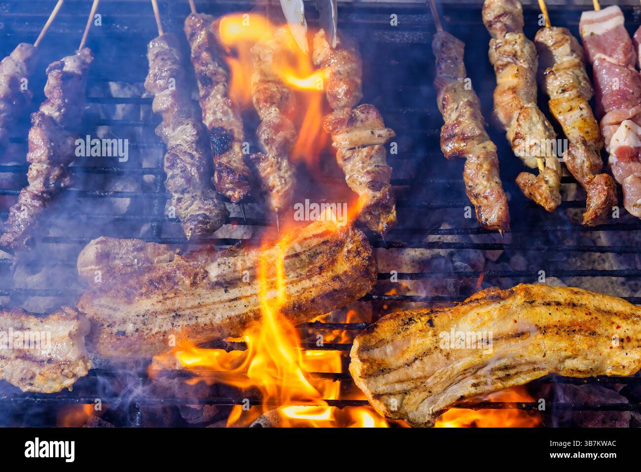 A grill filled with skewers and pork belly of meat cooking over open ...