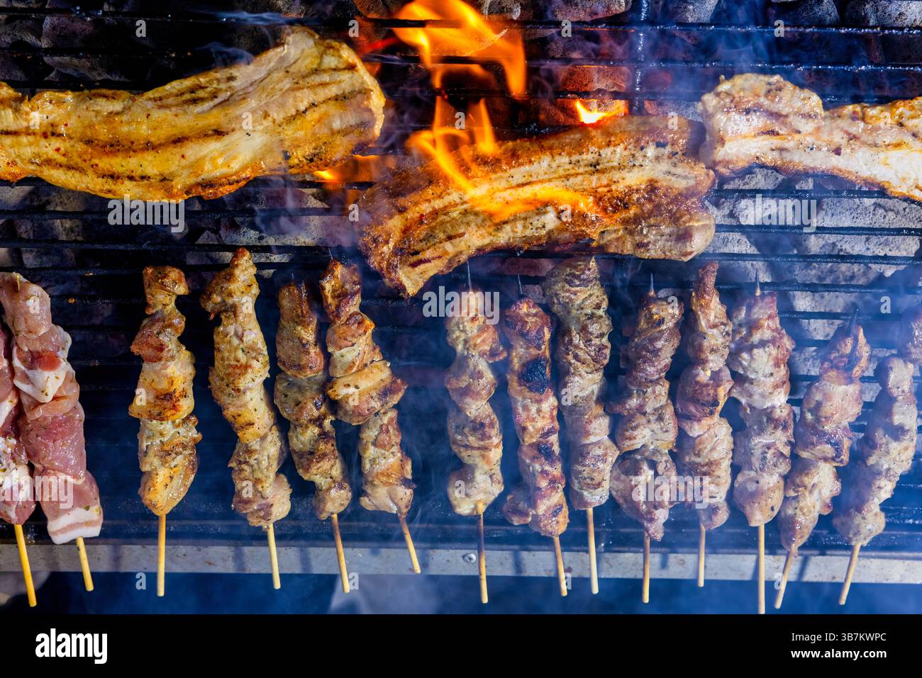 A grill filled with skewers and pork belly of meat cooking over open ...