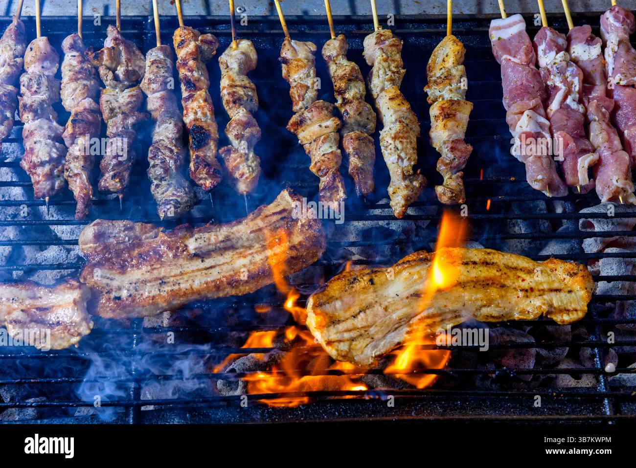 A grill filled with skewers and pork belly of meat cooking over open ...