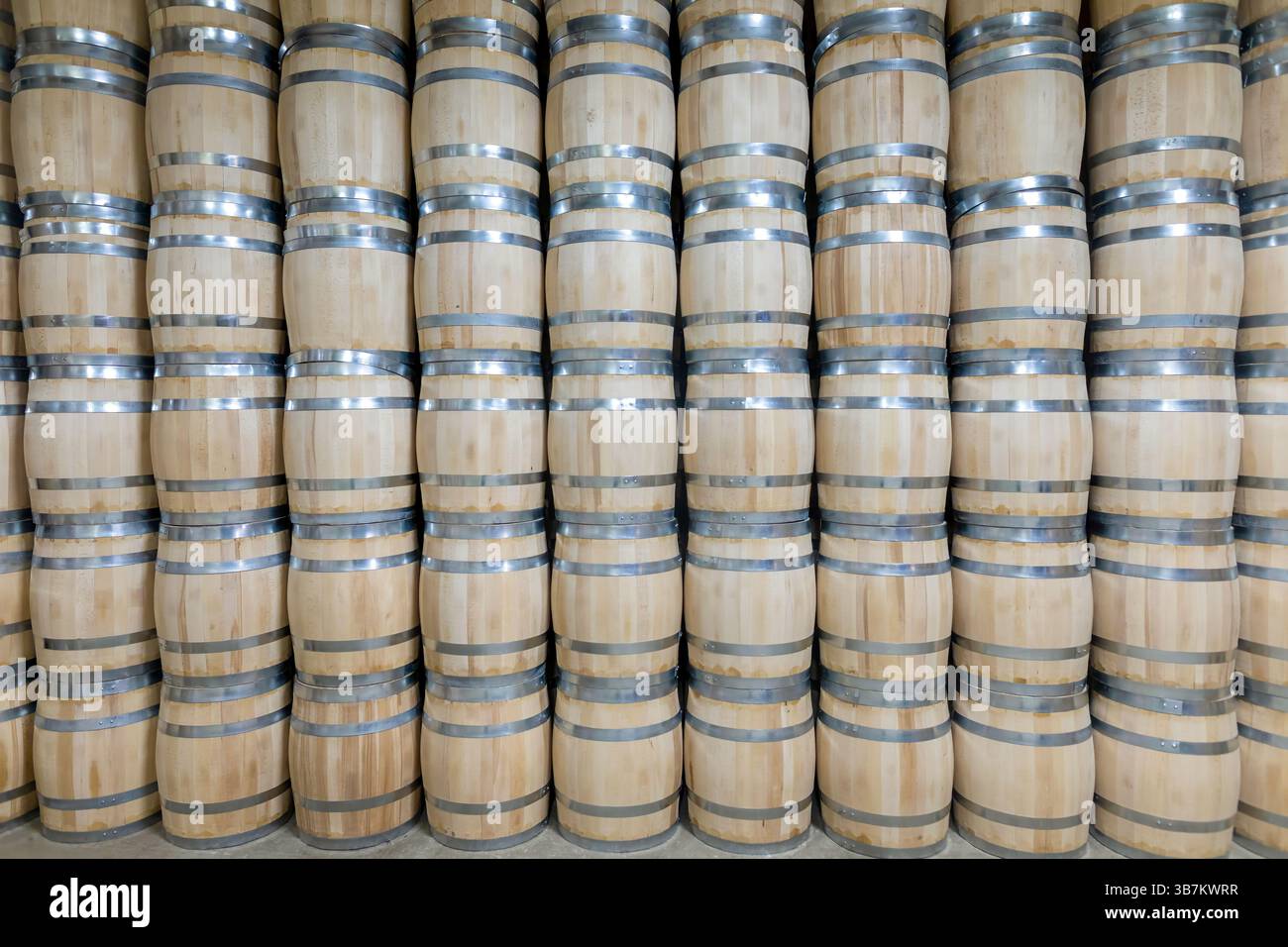 Rows of wooden barrels are neatly stacked in a storage area. Each ...