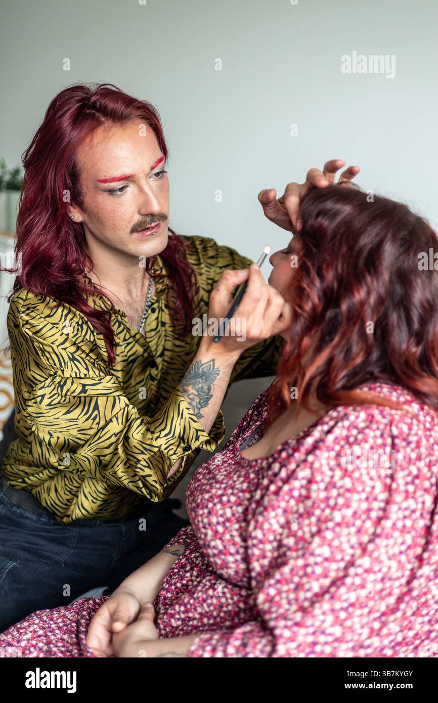Non-binary makeup artist with long red hair and a patterned shirt applying makeup on a curvy ...