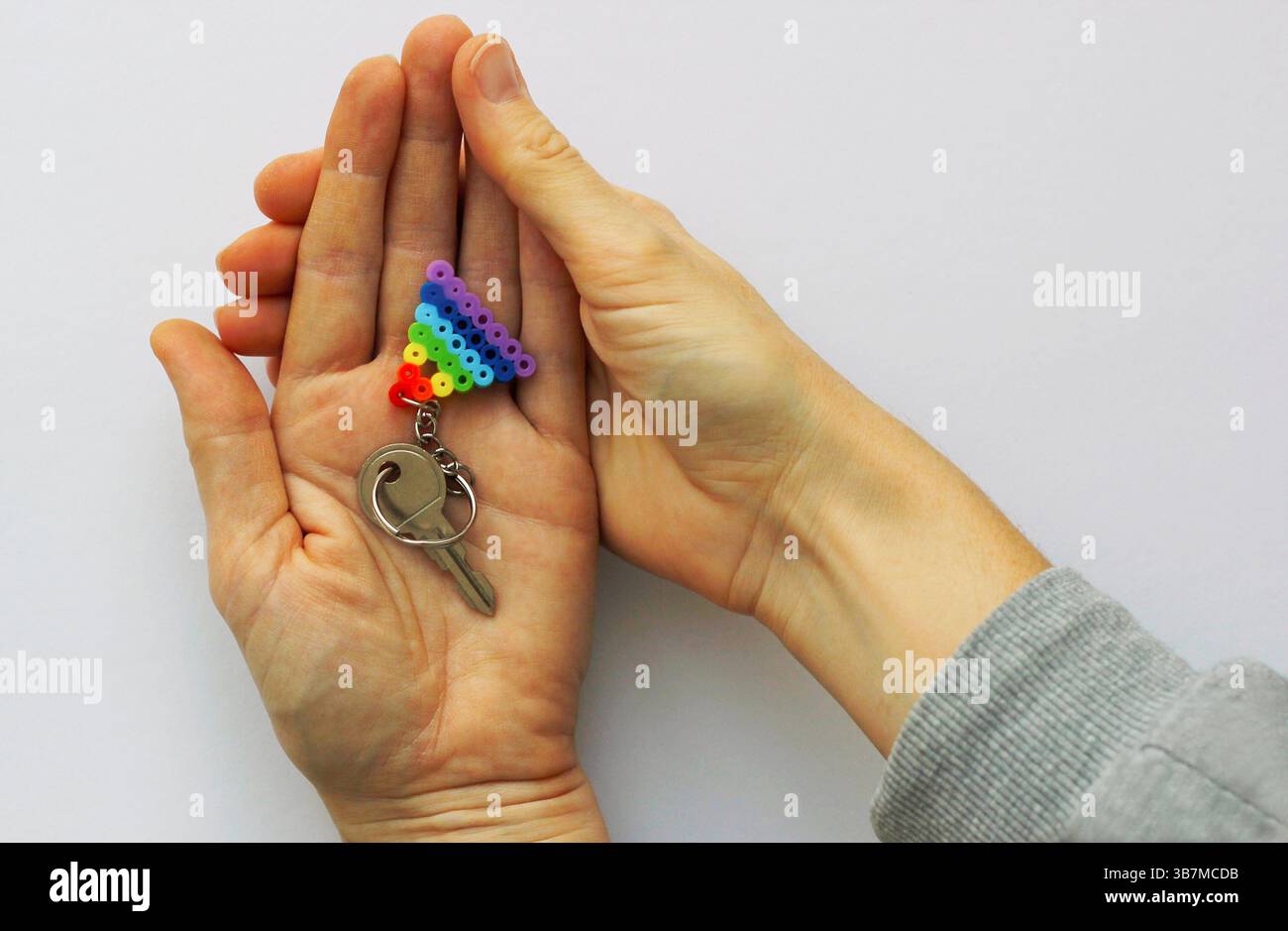 Two Caucasian female hands holding a silver key with a rainbow triangle ...