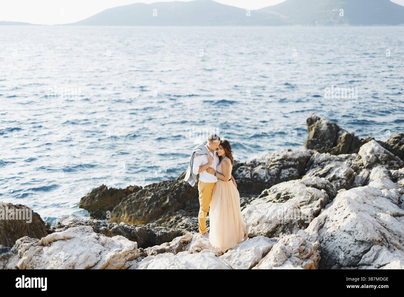 Handsome groom hugs cute smiling bride in pastel dress while standing ...