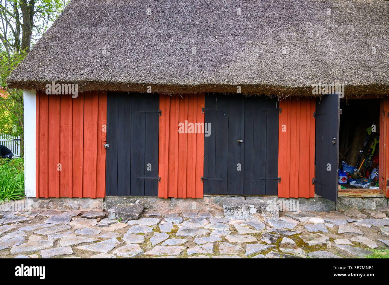 A rustic structure features a thatched roof and red wooden walls. Black ...