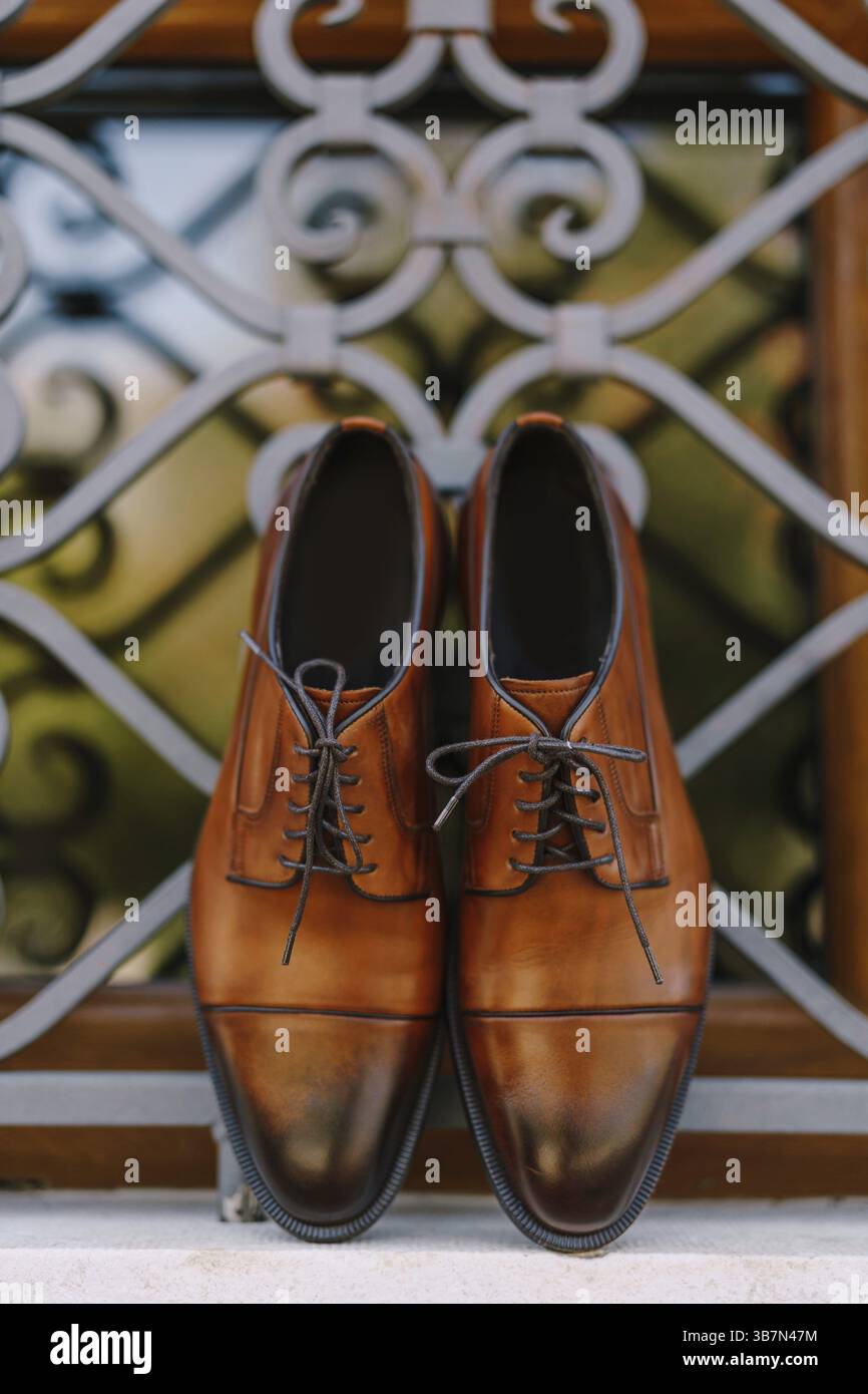 A close-up of new brown mens shoes against the metal bars of the window ...