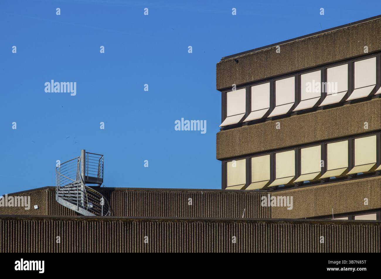 Spiral staircase on rooftop with modern brutalist architecture and blue ...