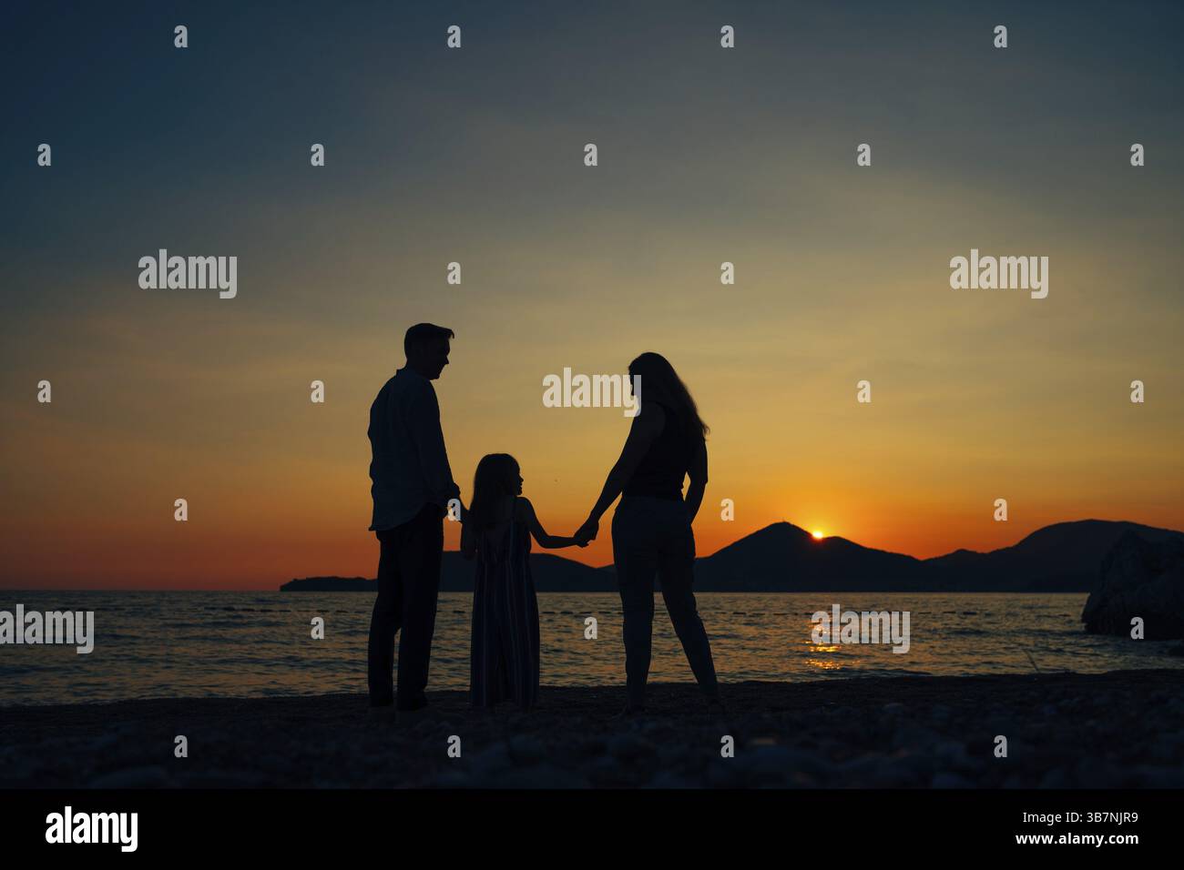Silhouettes of family of mom dad and daughter standing on the seashore ...