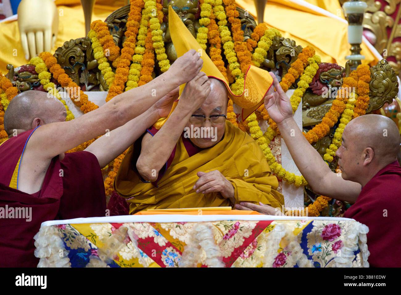 Attendant monks help their spiritual leader the Dalai Lama wear a ...