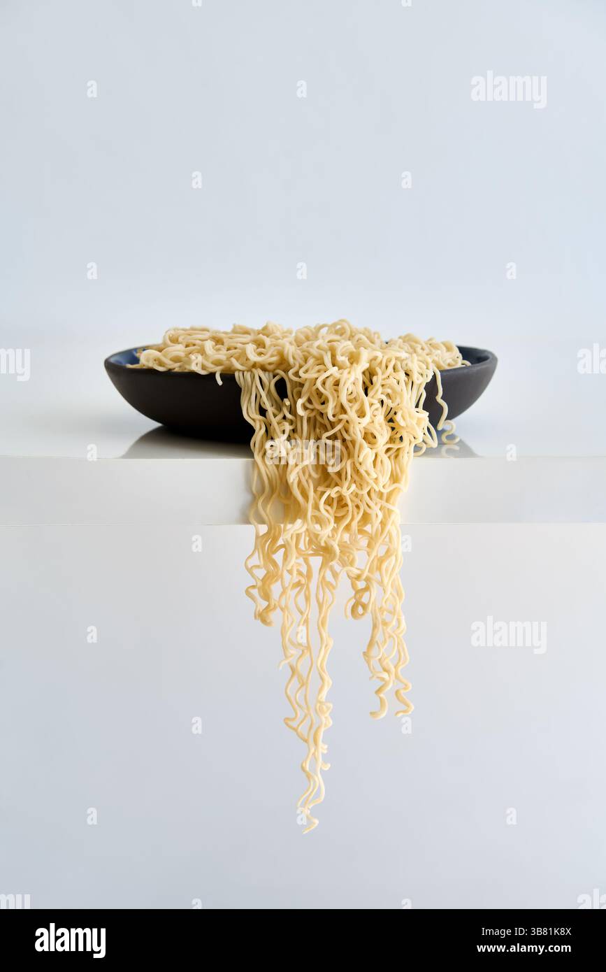 Cooked instant noodles overflow and spill from full bowl into table ...