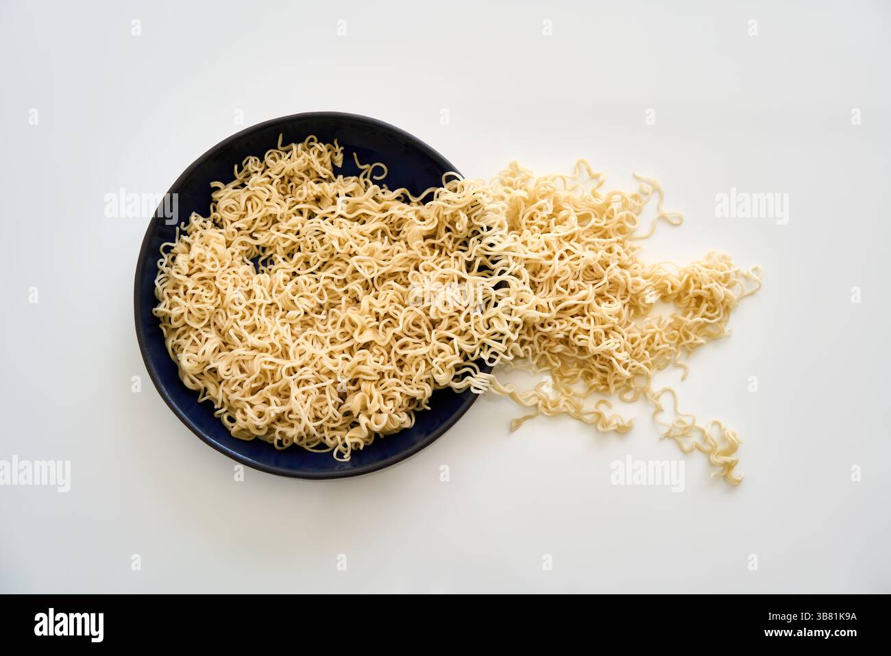Cooked instant noodles overflow and spill from full bowl into table ...