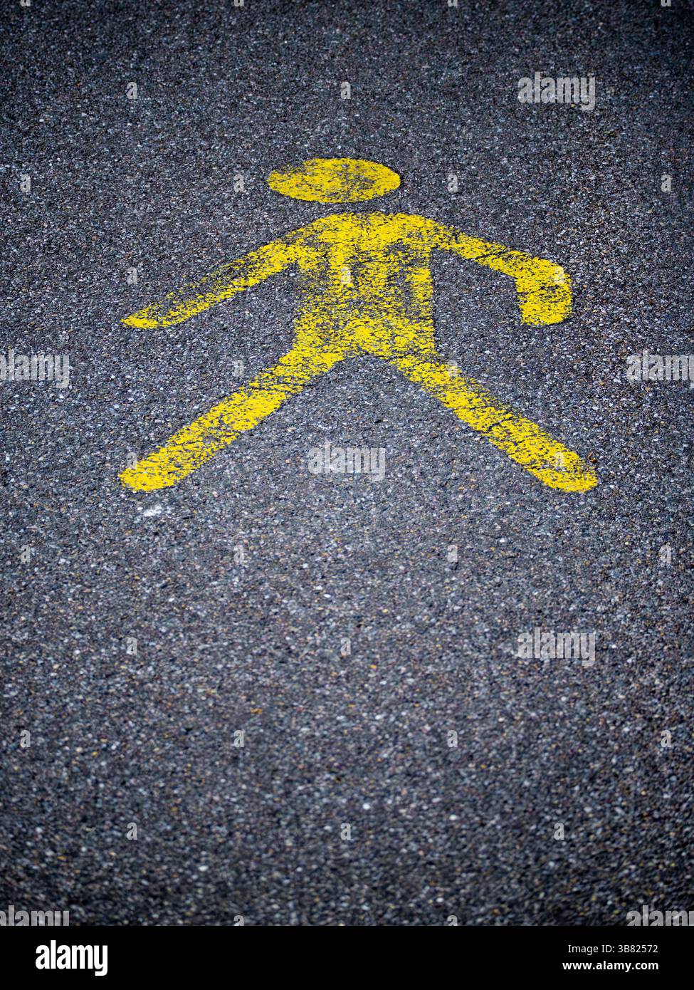A yellow pedestrian symbol painted on asphalt, indicating a walking ...