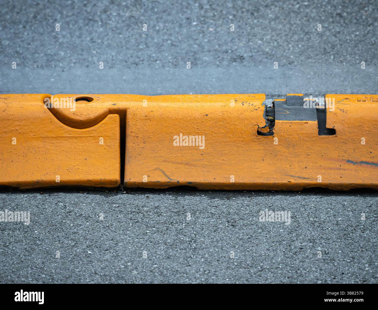 A close-up view of a yellow road barrier on a gray asphalt surface ...