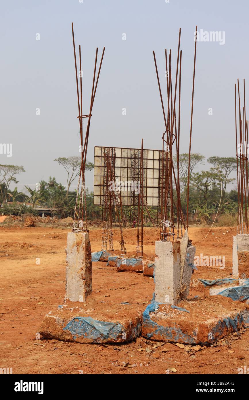 Concrete structures stand on reddish soil with exposed rusty metal ...