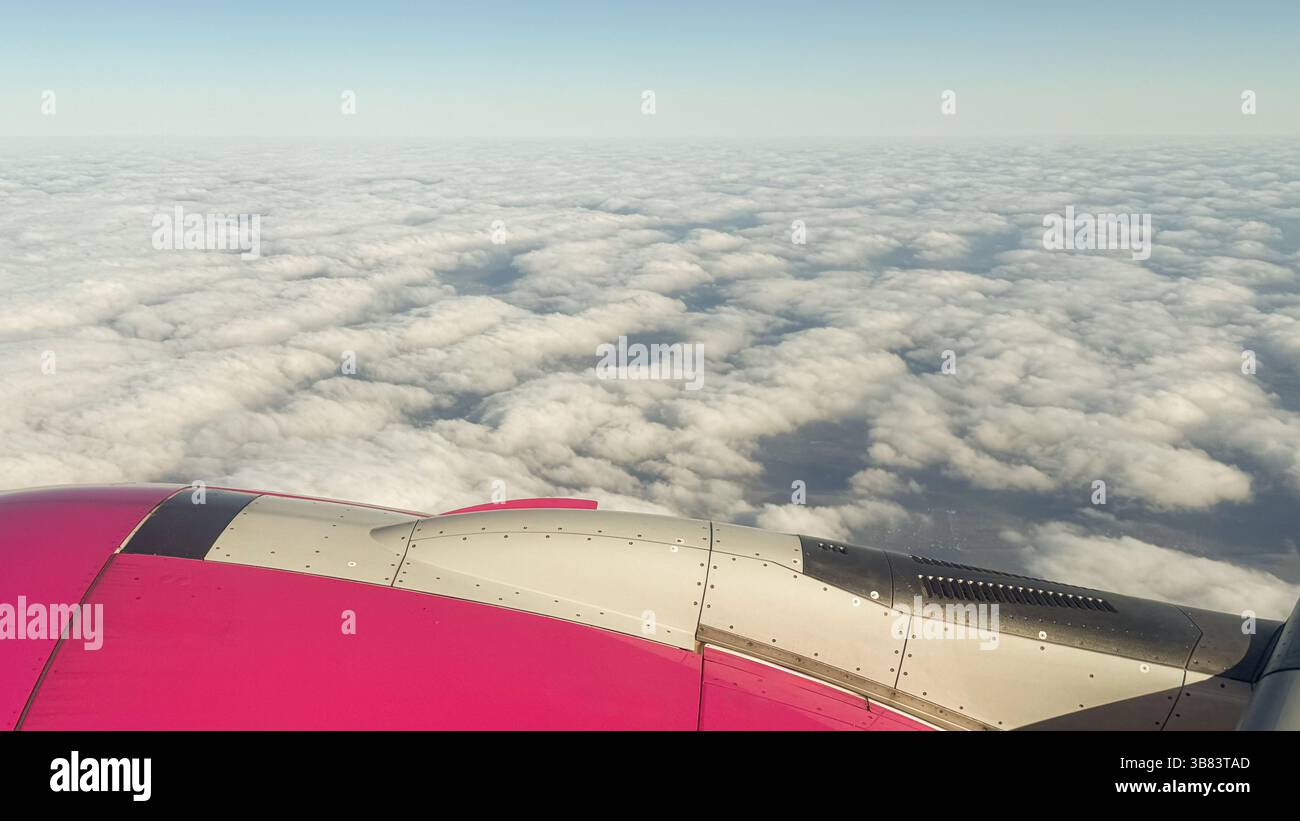Vibrant pink airplane wing over a vast sea of soft white clouds under a ...