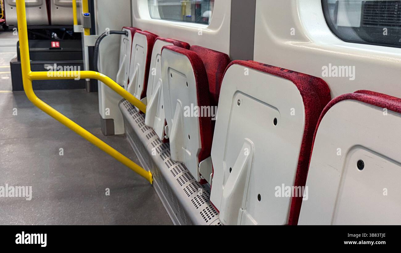 Folded red and white bus seats with yellow handrails inside an empty ...