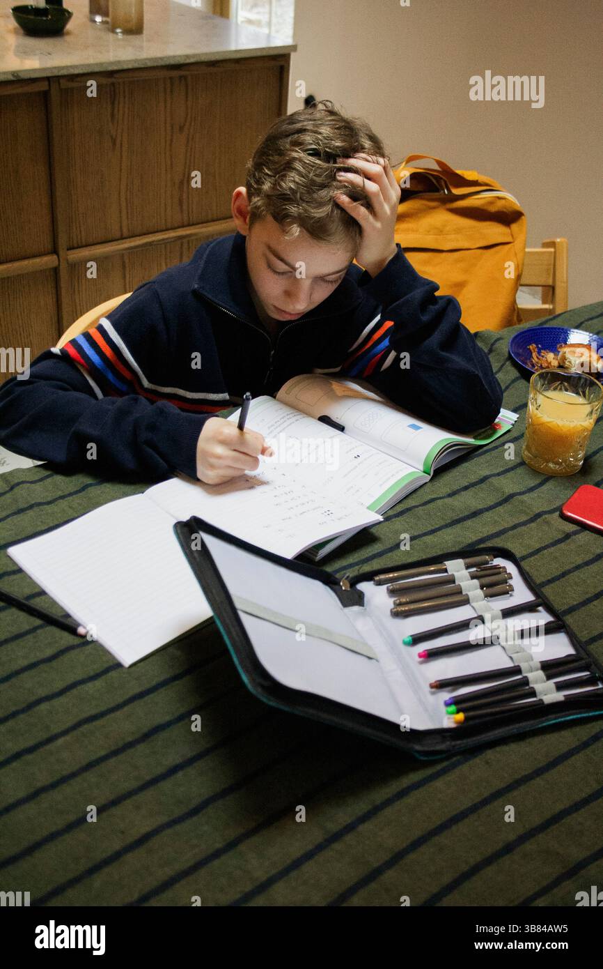 Depressed boy doing homework while sitting at dining table Stock Photo ...