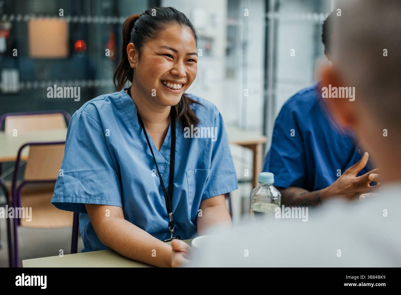 Happy female nurse wearing scrubs sitting with colleagues in hospital ...