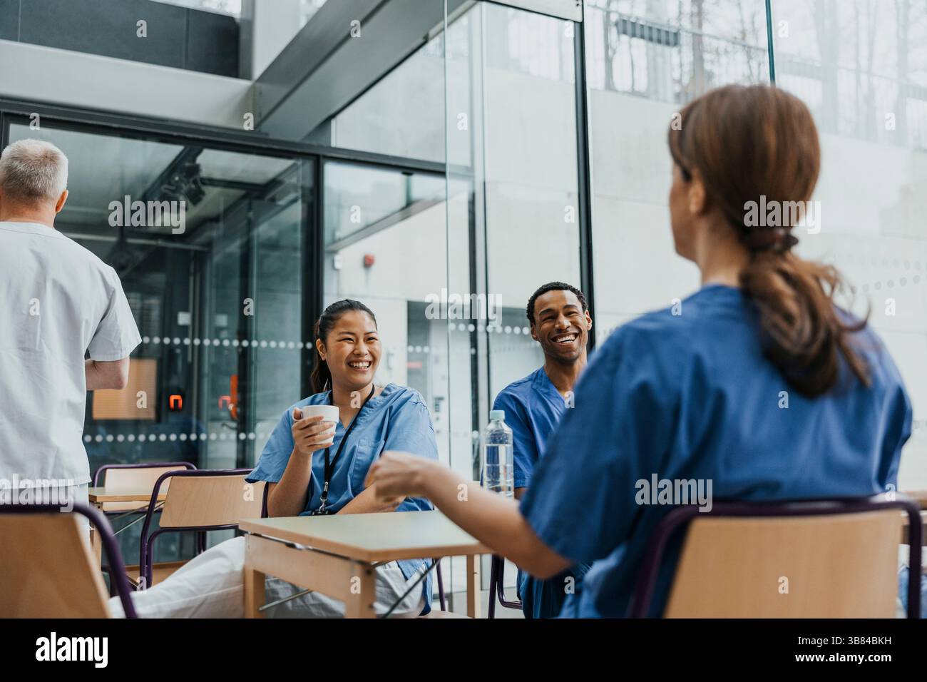 Happy multiracial male and female nurses sitting at table in cafeteria ...