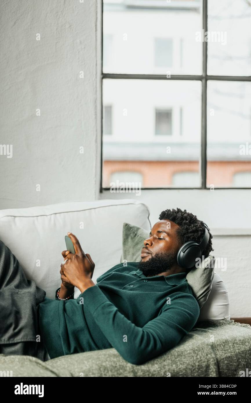 Relaxed businessman using smart phone while lying on sofa wearing ...