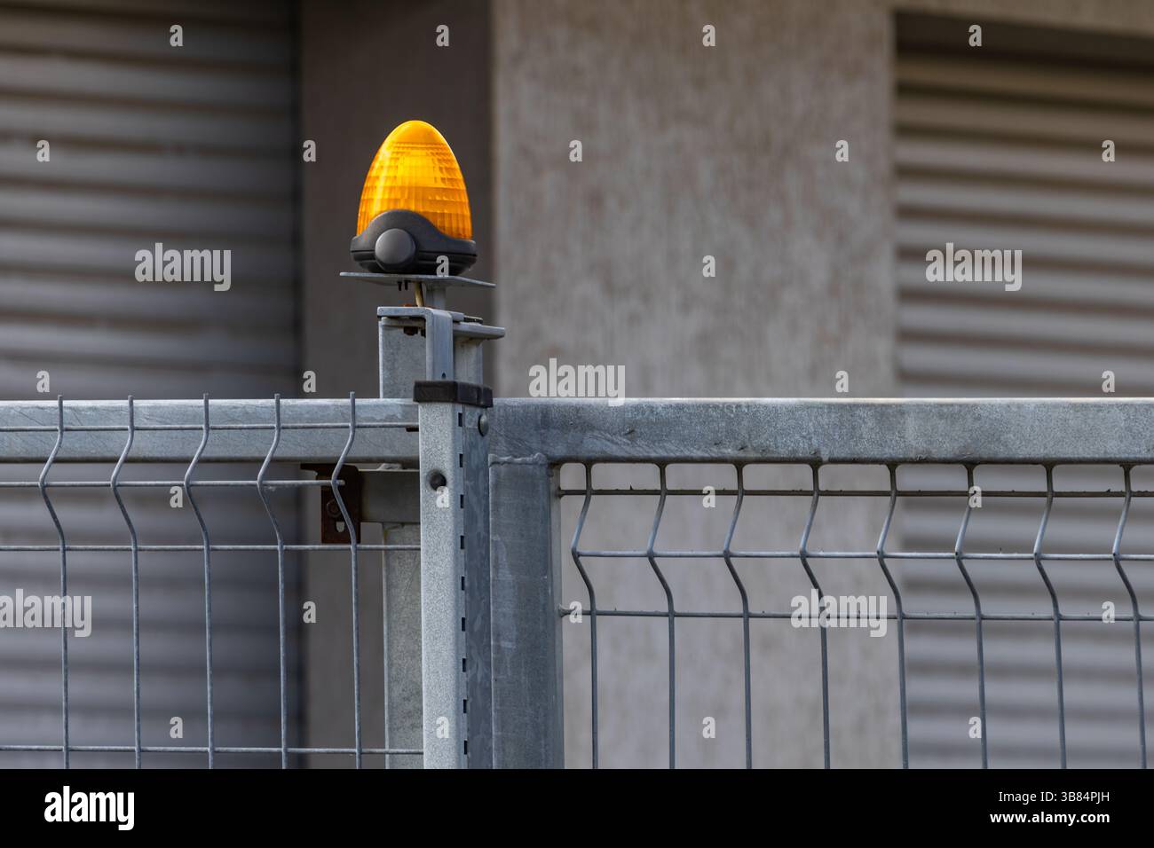 Orange warning lamp hanging on a metal electric sliding gate, warning ...