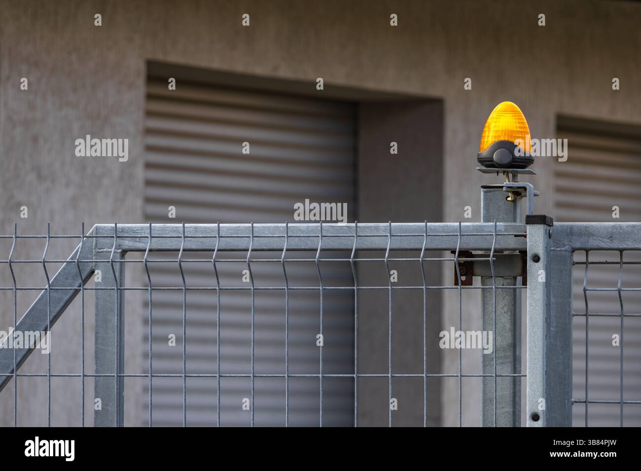 Orange warning lamp hanging on a metal electric sliding gate, warning ...