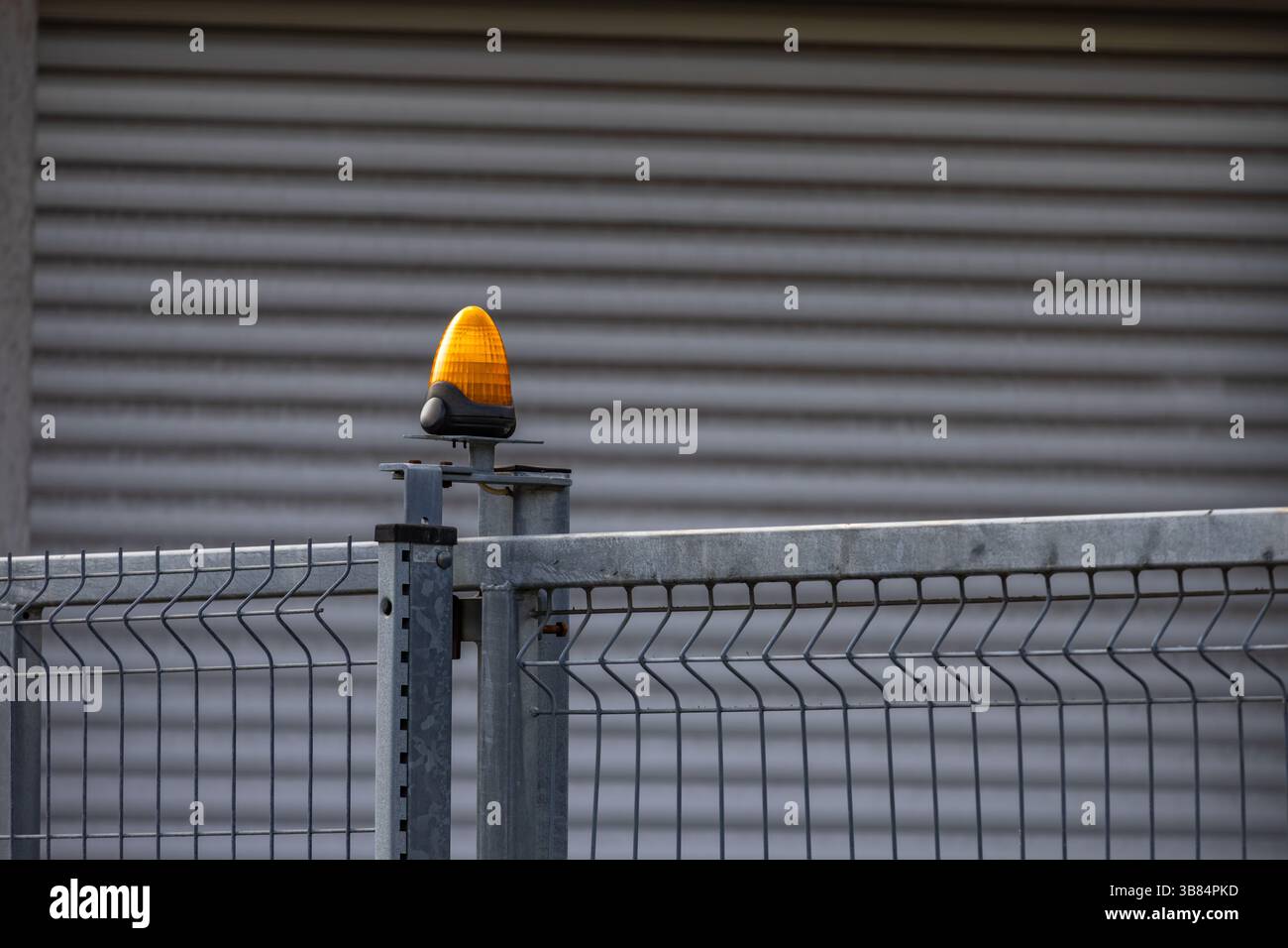 Orange warning lamp hanging on a metal electric sliding gate, warning ...
