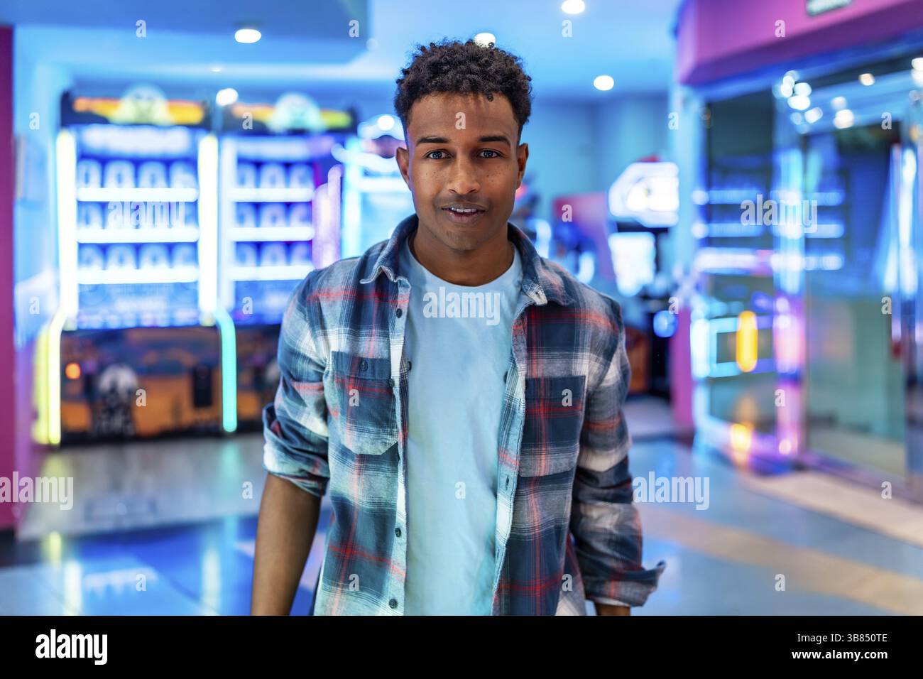 Young man smiles while standing in a lively arcade, surrounded by ...