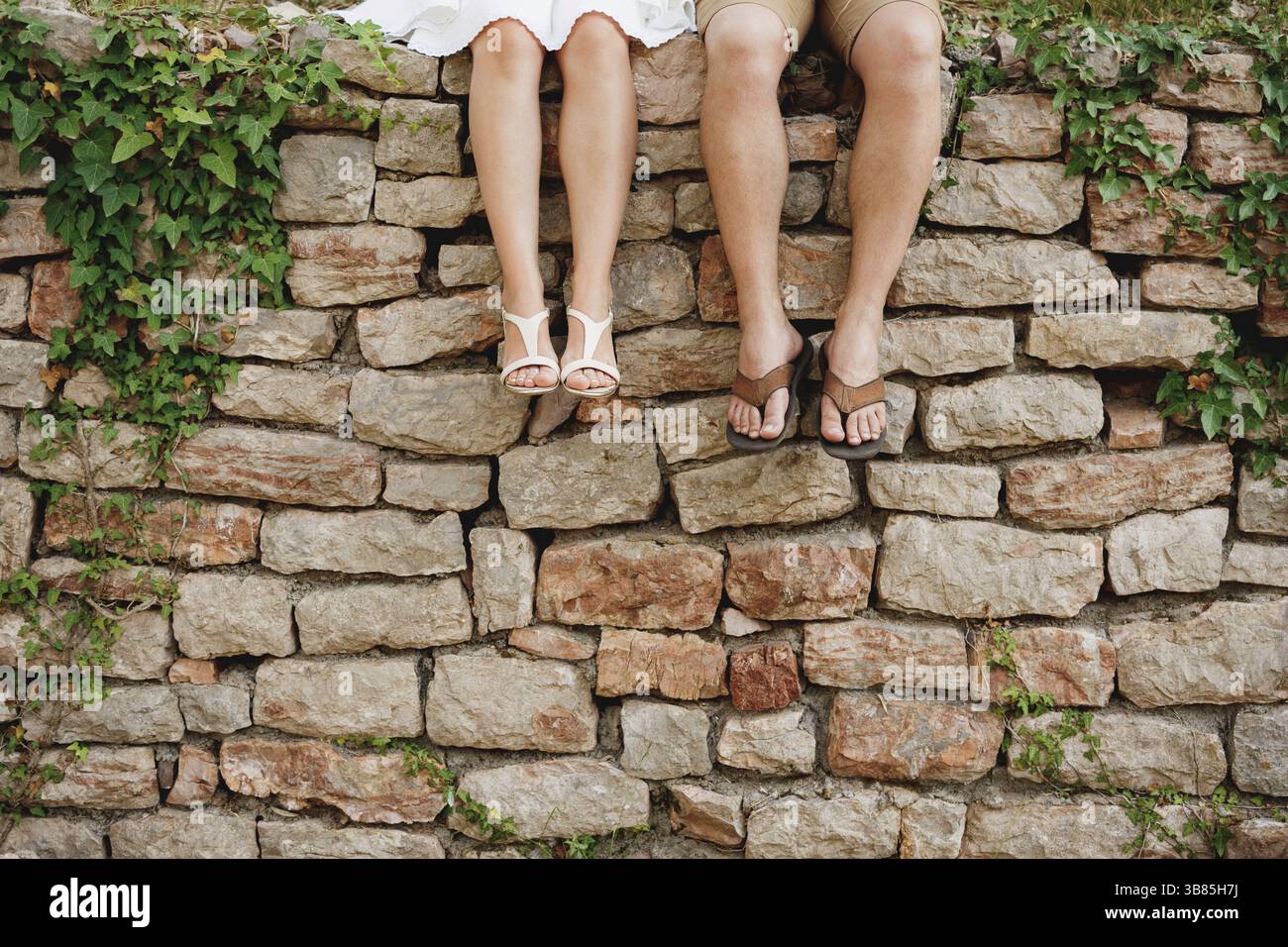 Legs of a man and a woman sitting side by side on the stone fence Stock ...