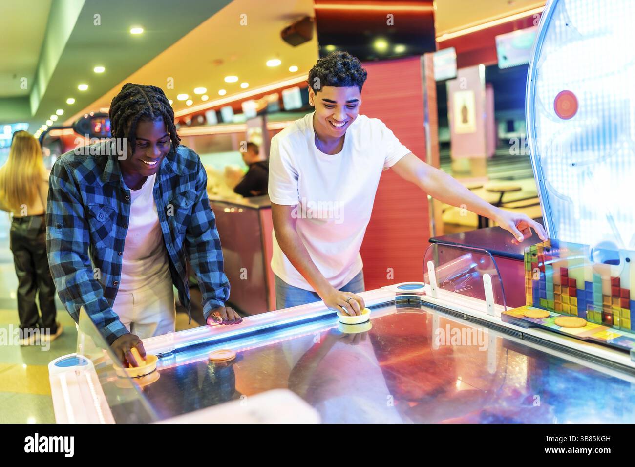Two young men are enjoying a friendly game of air hockey in a vibrant bowling alley arcade Stock ...