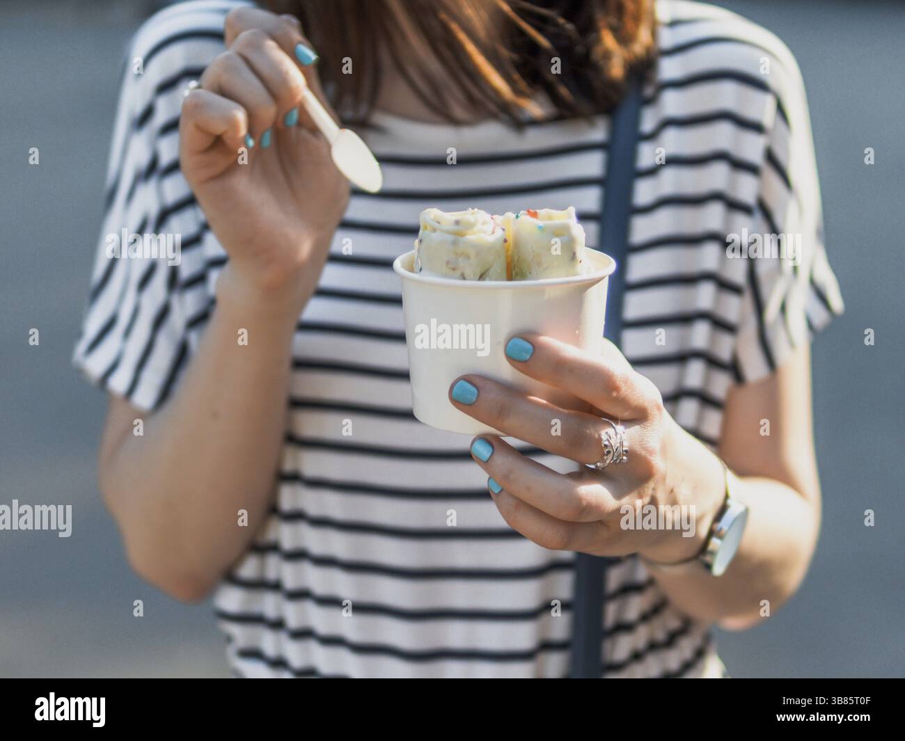 Rolled ice cream in cone cup in woman hands. Woman in striped dress ...